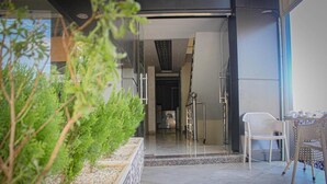 Entrada moderna de hotel com porta de vidro, um pequeno jardim interno e uma área de estar com cadeiras.
