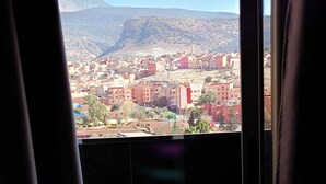 Vista da janela com cortinas, mostrando um horizonte urbano com edifícios e uma montanha ao longe.