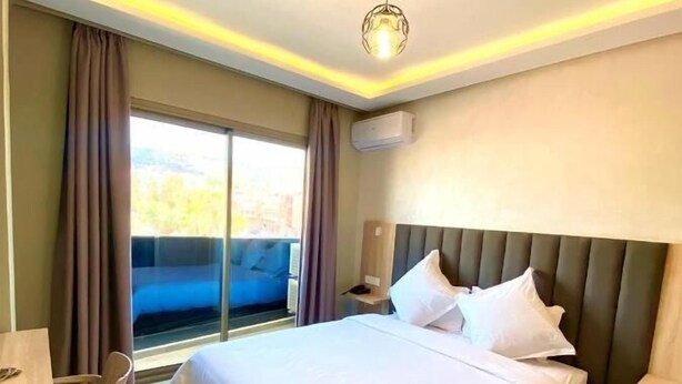 Quarto de hotel moderno com uma cama grande, uma escrivaninha e vista para a cidade pela janela.