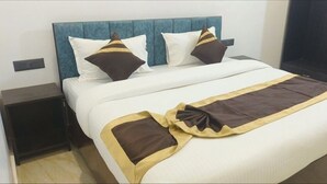 Cama bem arrumada com cabeceira azul, roupa de cama branca e marrom, e um corredor decorativo marrom e dourado.