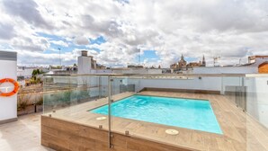 Piscina no terraço com guarda-corpos de vidro, um salva-vidas e vista para a paisagem urbana.