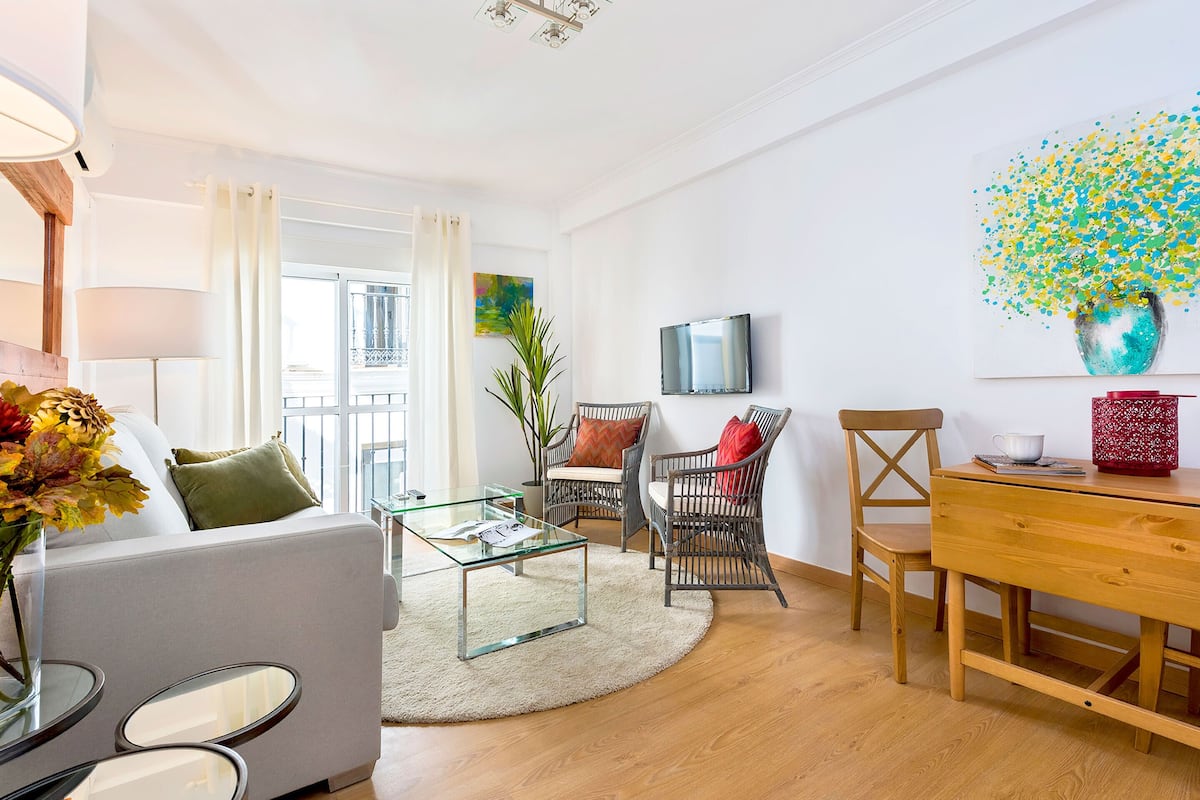 Uma sala de estar moderna com sofá, mesa de centro, cadeiras, TV e um quadro.