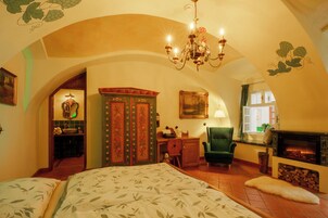 Quarto com cama grande, escrivaninha, cadeira, lareira e lustre.