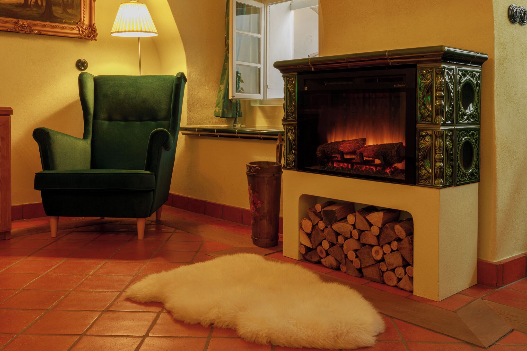 Um quarto acolhedor com uma poltrona verde, uma lareira com espaço para lenha e um tapete de pele branca no chão.