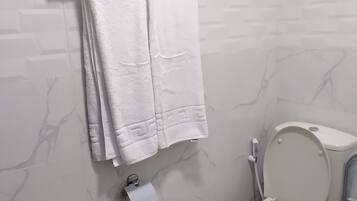 Casa de banho com sanita, um porta-toalhas com duas toalhas e rolo de papel higiénico.