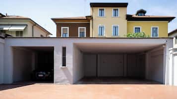 Um edifício residencial com garagem, um carro estacionado e uma pequena varanda.