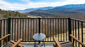 Um terraço com uma mesa e duas cadeiras, com vista para uma paisagem montanhosa.
