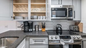 Uma cozinha moderna com armários brancos, micro-ondas, fogão, chaleira e torradeira.