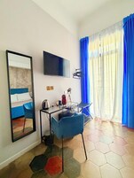 Quarto de hotel com uma cama, uma escrivaninha com cadeira, televisão e janela com cortinas azuis.