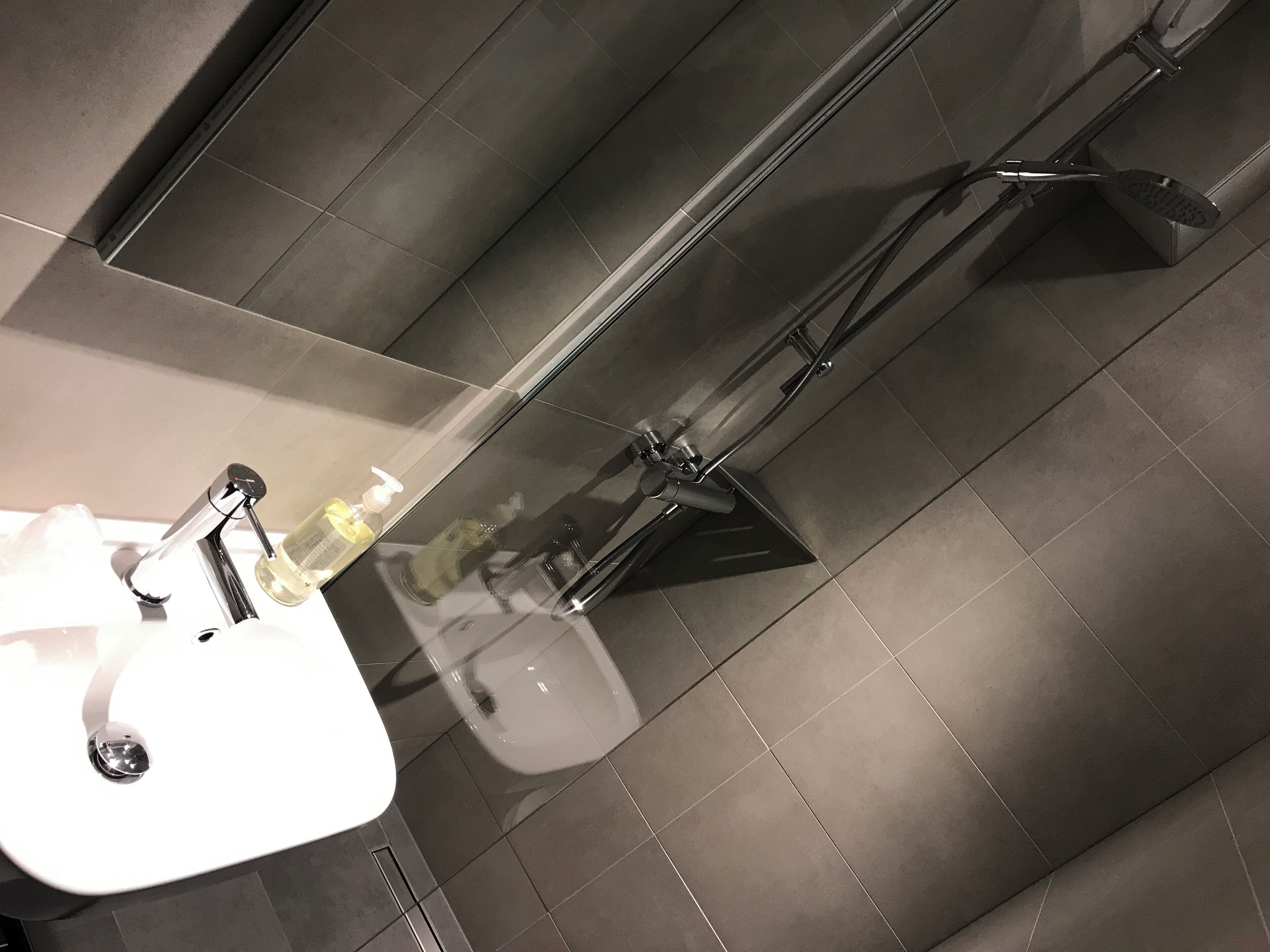 Casa de banho moderna com lavatório branco, chuveiro manual e cabine de duche em vidro.