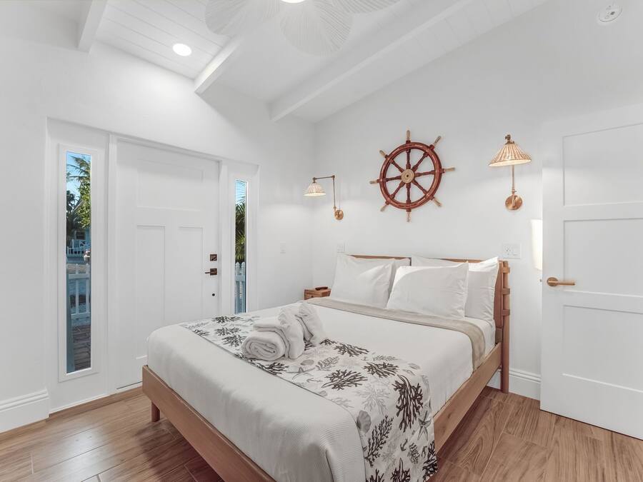 Quarto com cama grande, decoração em forma de leme de navio, duas luminárias na parede e uma porta de vidro deslizante para uma varanda.