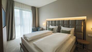 Quarto de hotel com duas camas, uma cadeira, uma mesinha e uma televisão.
