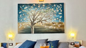 Quarto de hotel com cama, almofadas, um quadro, um copo de sumo de laranja e toalhas.