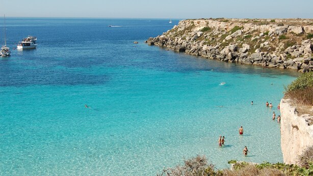 Uma paisagem costeira com águas azul-turquesa cristalinas, falésias rochosas e barcos.