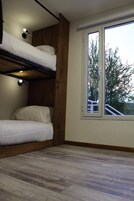 Quarto com beliche, janela grande, paredes de madeira e luminária.