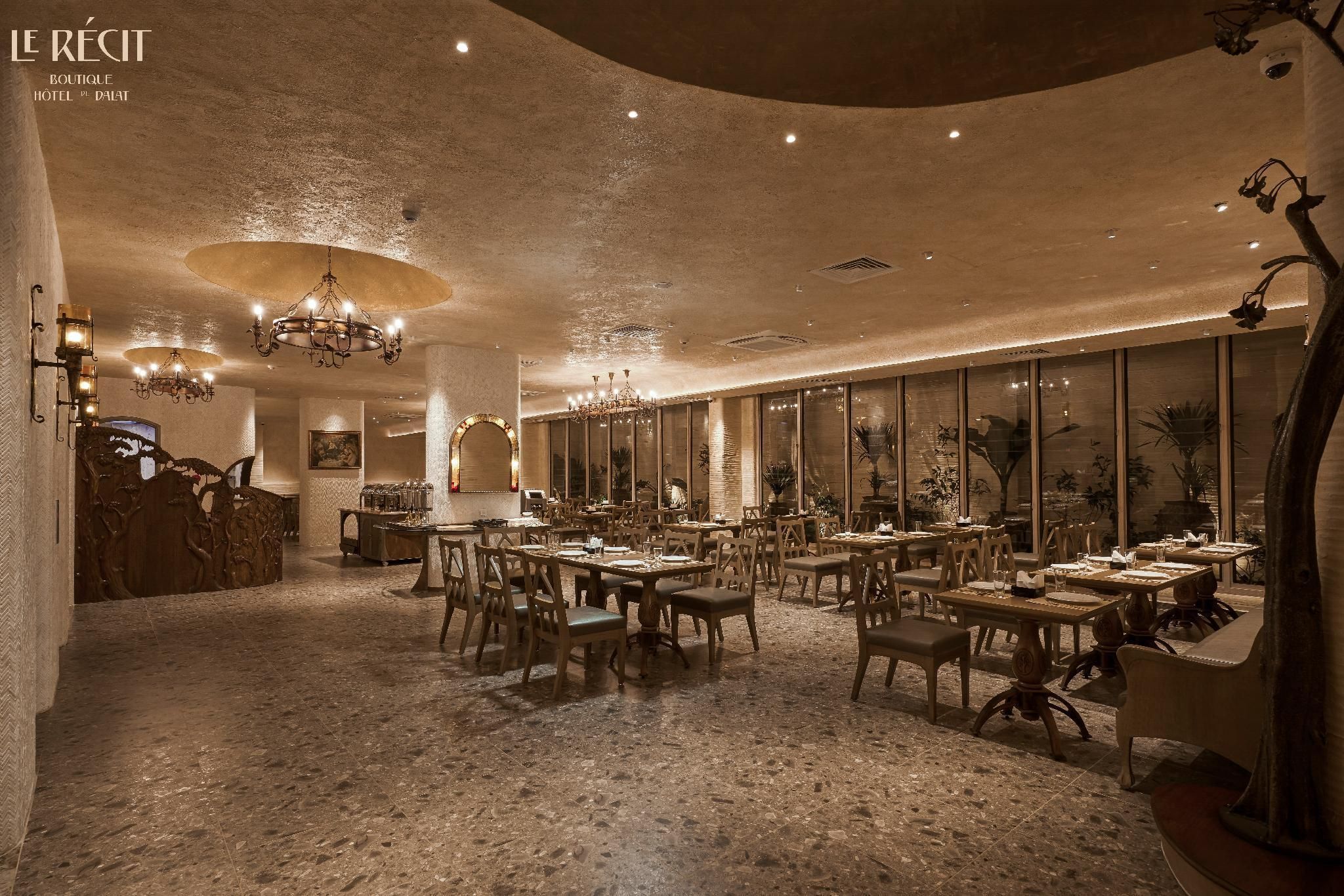 Uma sala de jantar ampla e elegantemente decorada, com várias mesas e cadeiras, lustres e janelas grandes que oferecem vista do interior.