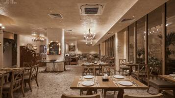 Um restaurante amplo com tetos altos, lustres e uma paleta de cores quentes. Mesas estão dispostas para refeições, e o chão é revestido com azulejos.