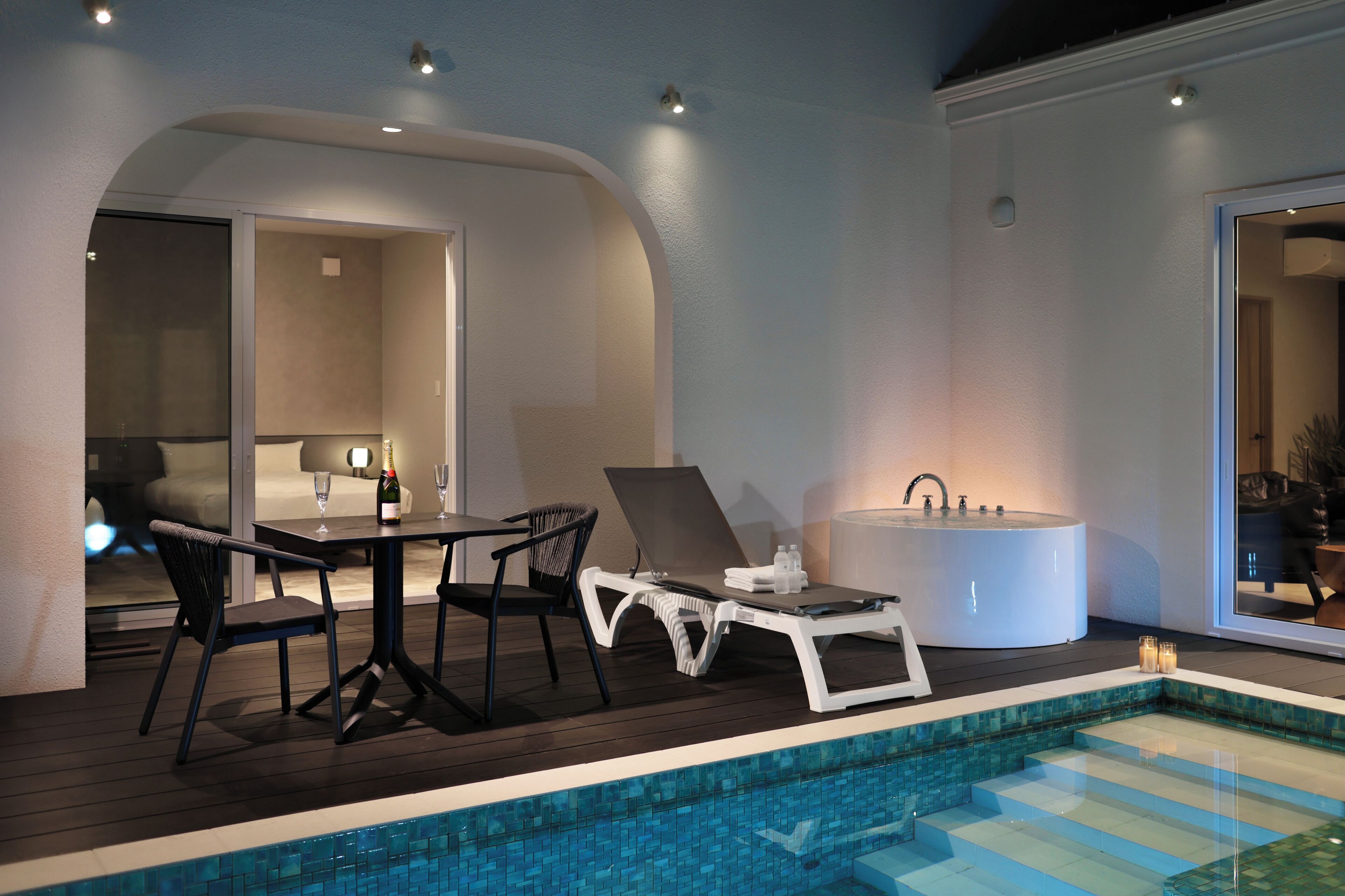 Uma área de piscina moderna ao ar livre com espreguiçadeira, mesa com uma garrafa de vinho e banheira de hidromassagem.