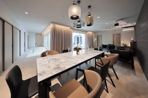 Uma área de refeições moderna com mesa de mármore, cadeiras pretas e bege, e iluminação pendente.