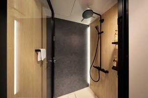 Casa de banho moderna com chuveiro de efeito chuva, chuveiro manual e um frasco de champô numa prateleira.
