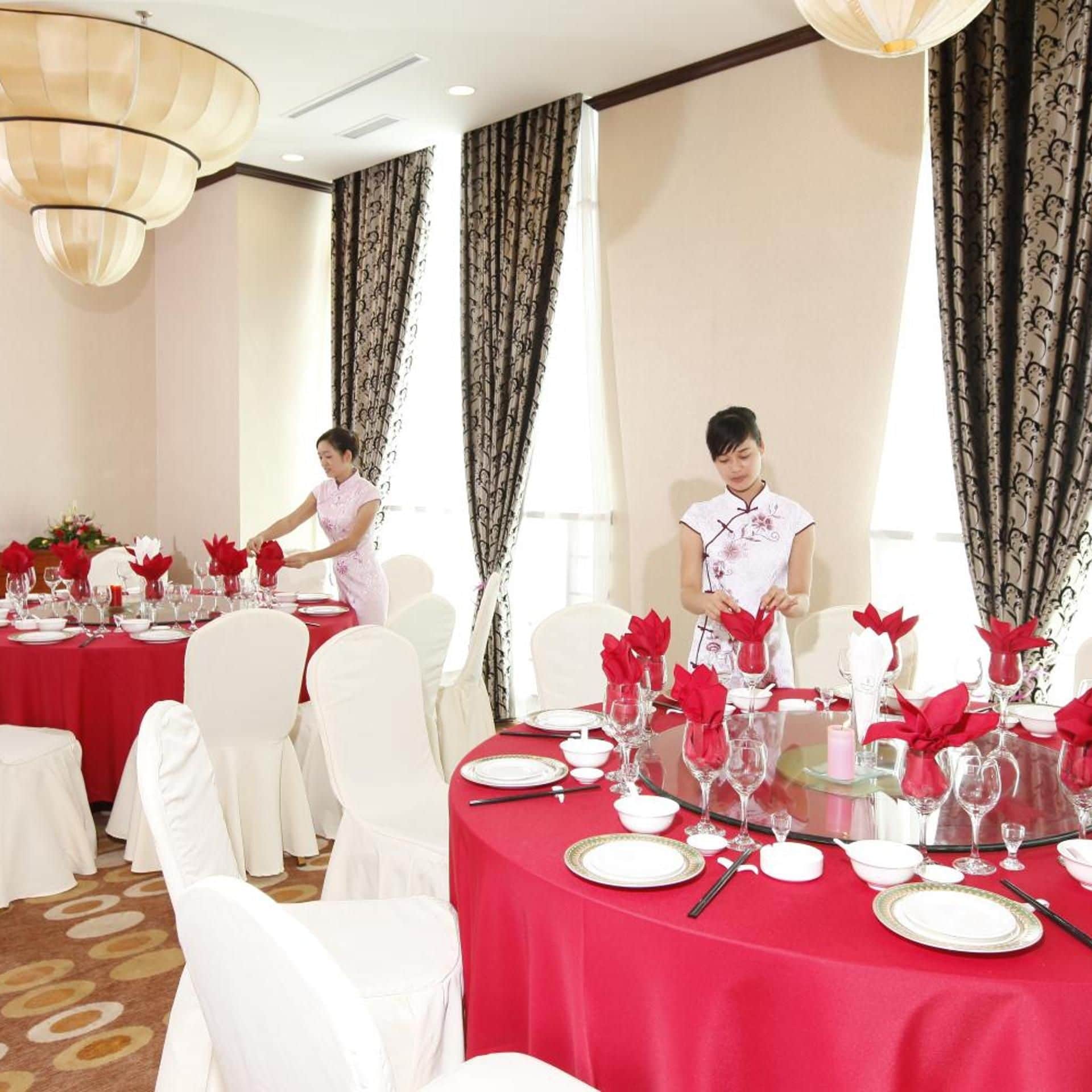 Uma sala de banquetes com mesas montadas para um evento formal, com toalhas vermelhas, cadeiras brancas e arranjos florais.