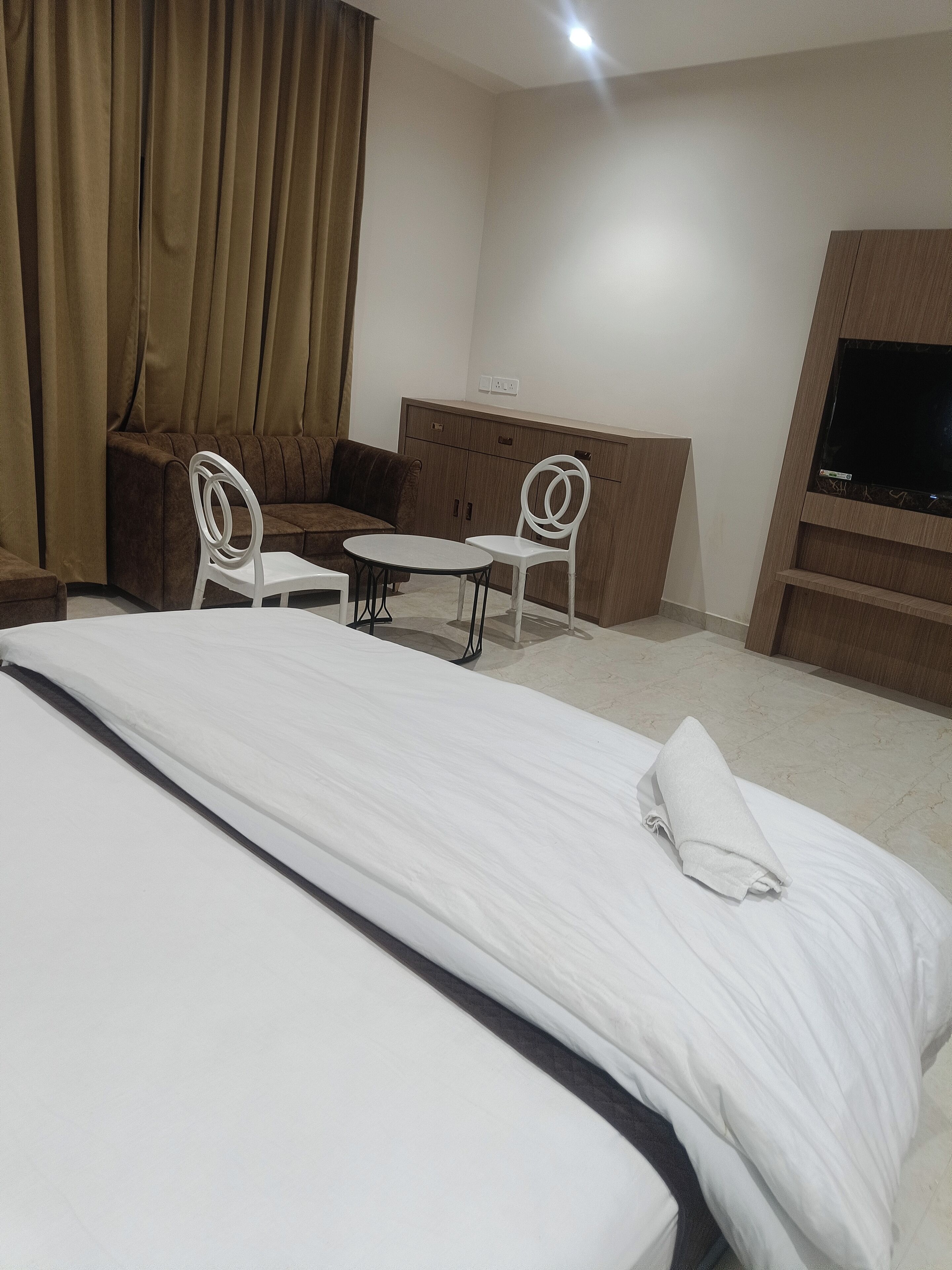 Quarto de hotel com uma cama grande, uma mesinha, duas cadeiras, um sofá, uma TV e um armário.
