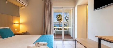 Quarto de hotel com cama, um banco, TV e varanda com vista.