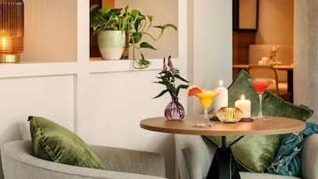 Um espaço de estar aconchegante com uma mesa redonda, almofadas verdes, um vaso com flores e uma vela.
