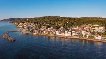 Uma cidade costeira com edifícios ao longo da orla, um molhe rochoso e colinas ao fundo.
