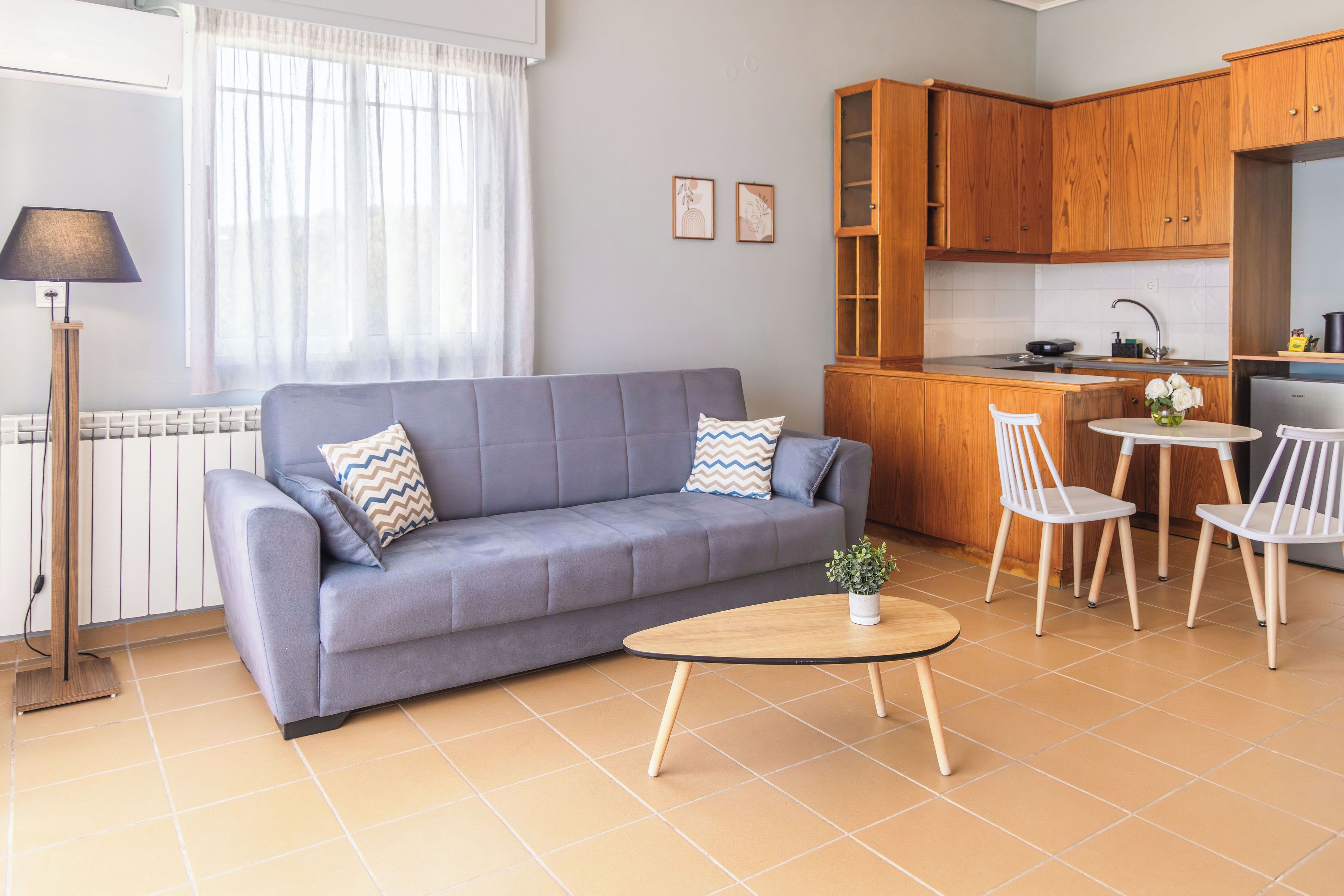 Uma sala de estar moderna com sofá, uma mesinha redonda e uma área de cozinha com armários de madeira e um conjunto de jantar.