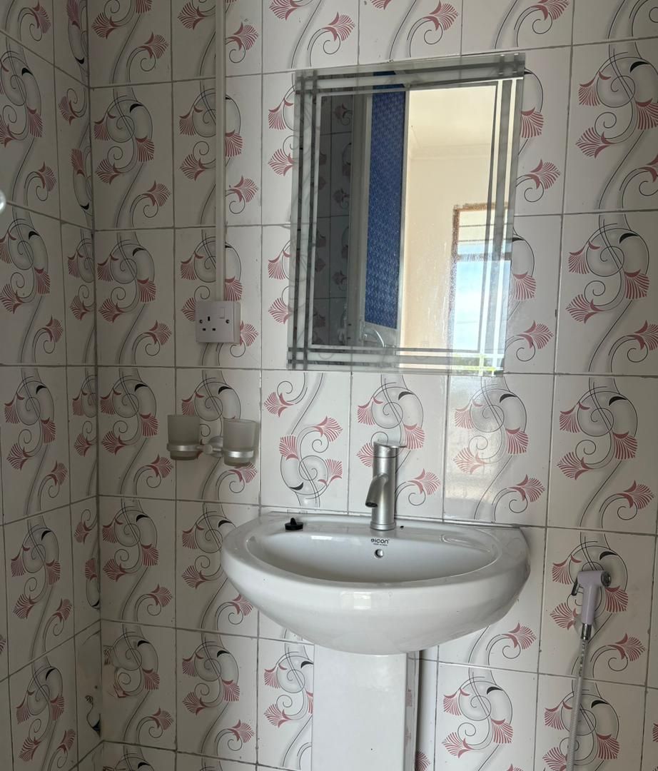 Um banheiro com pia branca, espelho e parede com padrão de azulejos florais.