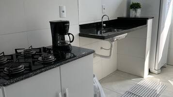 Uma cozinha moderna com armários brancos, bancada preta, cafeteira, fogão a gás, pia de aço inoxidável e uma geladeira.
