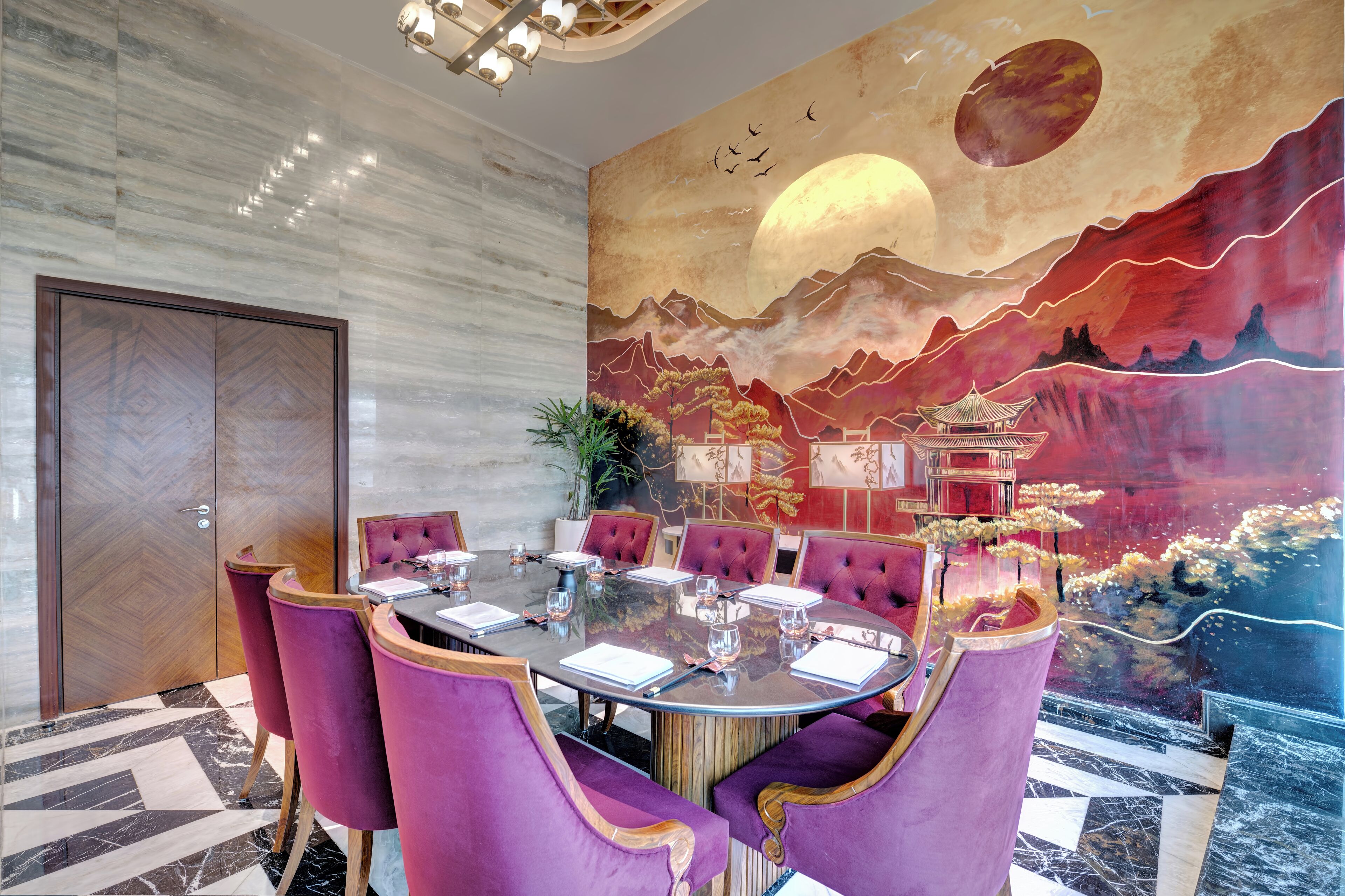 Sala de conferências com uma mesa redonda, cadeiras roxas e um mural de uma paisagem com montanhas e uma lua.