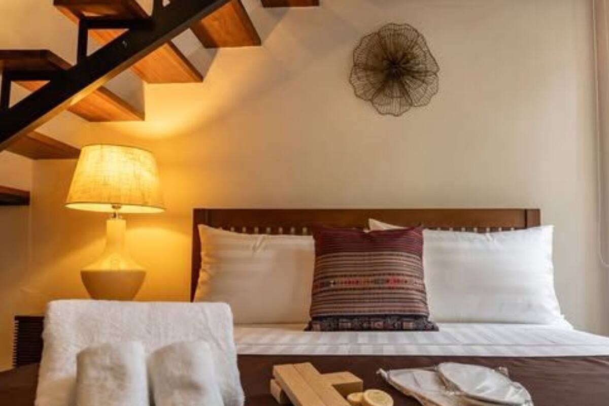 Quarto de hotel com uma cama, abajur, um detalhe decorativo na parede e uma janela.