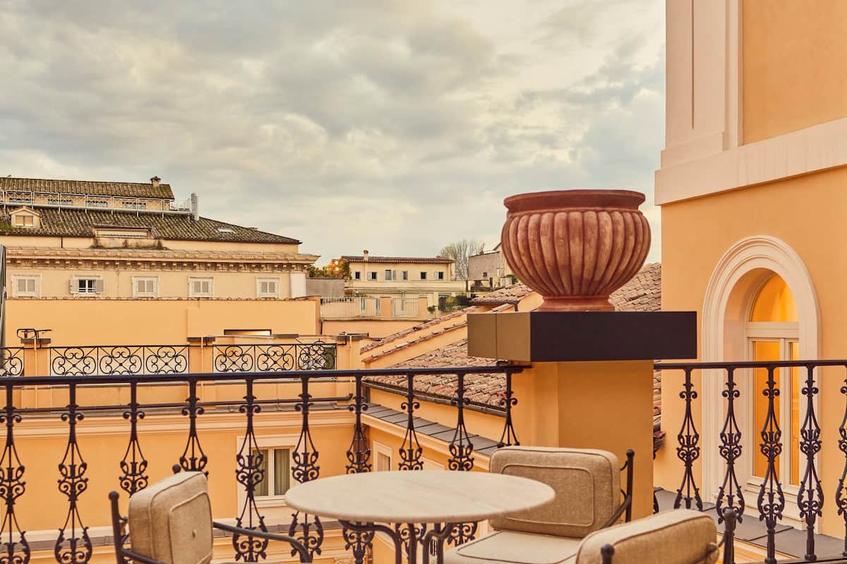 Um terraço com uma mesa redonda e quatro cadeiras, um vaso de terracota grande e vista para edifícios sob um céu nublado.