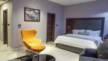 Quarto de hotel moderno com uma cama grande, uma poltrona amarela vibrante, uma pequena mesa redonda e um quadro na parede.