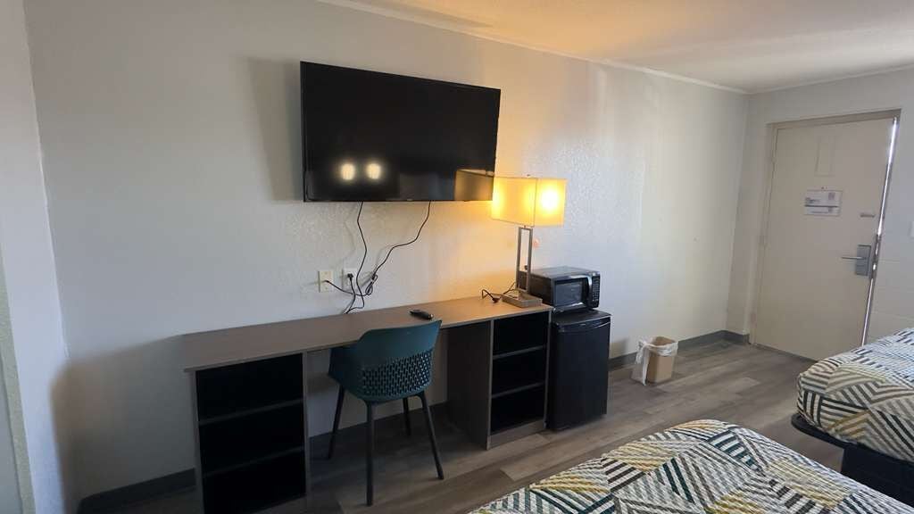 Quarto de hotel com escrivaninha, cadeira, televisão e duas camas.