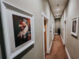 Corredor com obras de arte emolduradas nas paredes, piso coberto por carpete e portas que dão acesso a outros cômodos.