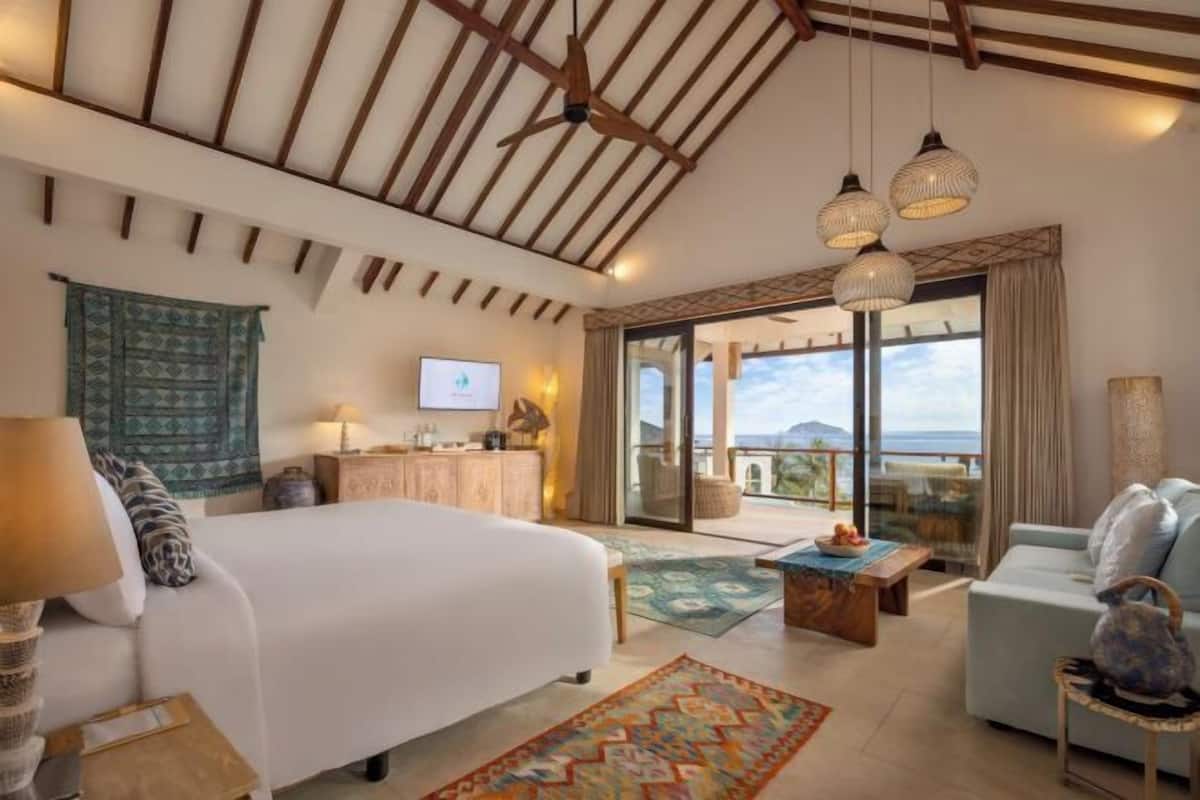 Quarto com cama grande, escrivaninha, sofá e varanda com vista.
