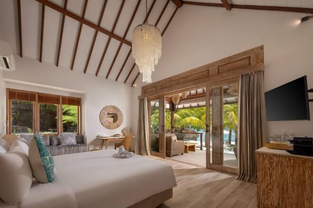 Um quarto espaçoso com uma cama grande, uma escrivaninha e vista para uma área tropical ao ar livre.