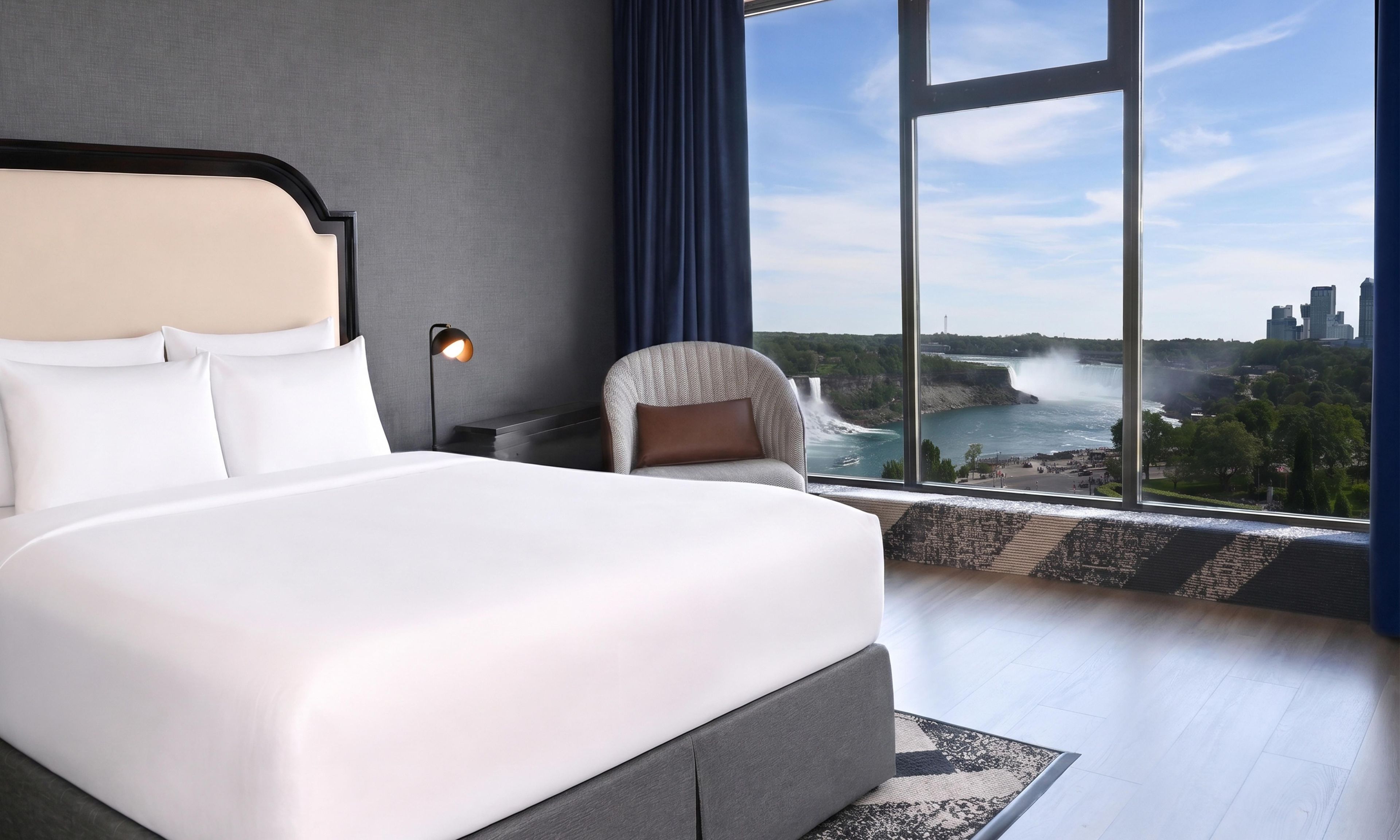 Quarto de hotel moderno com uma cama grande, vista para uma cachoeira e para o horizonte da cidade.
