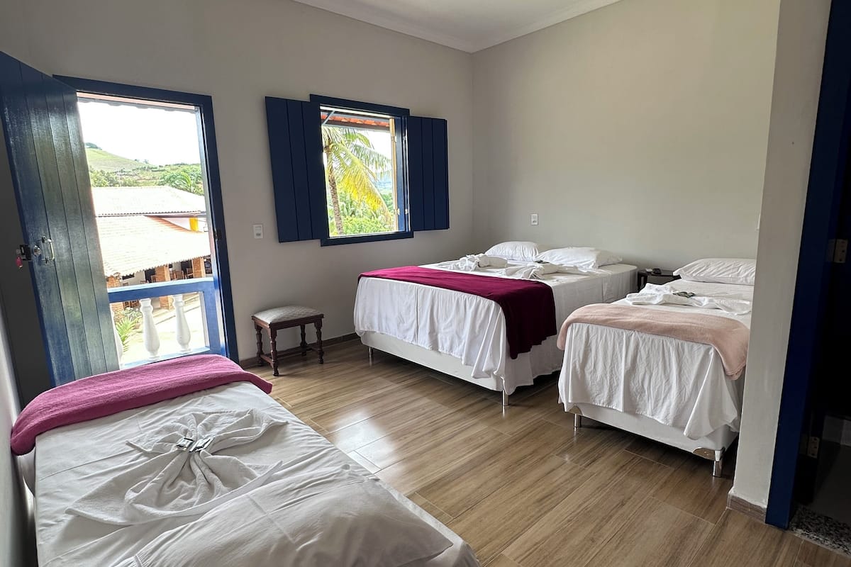 Quarto de hotel com duas camas, uma janela com vista para o verde e piso de madeira.