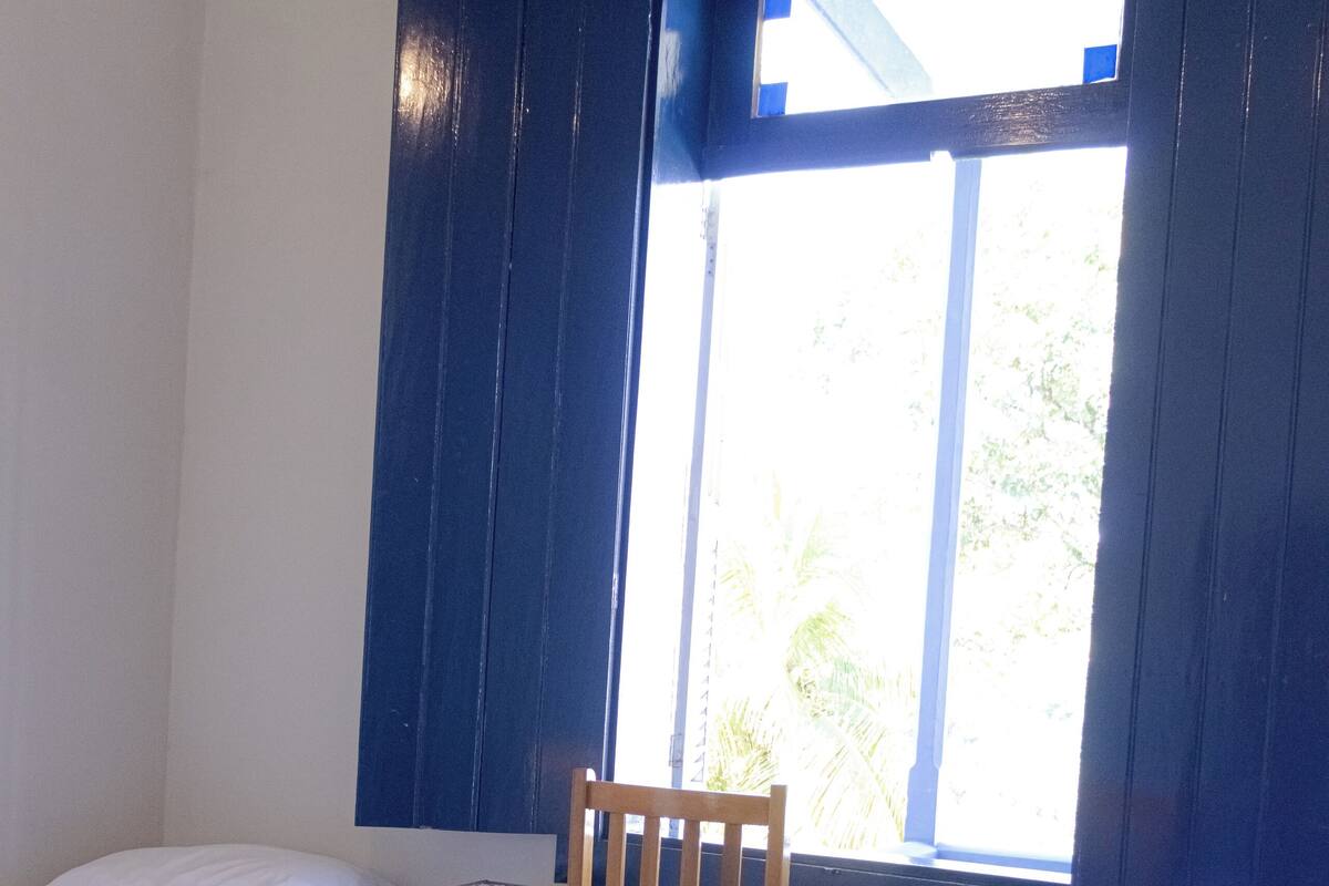 Quarto com duas camas, uma cadeira de madeira e uma janela com persianas azuis.