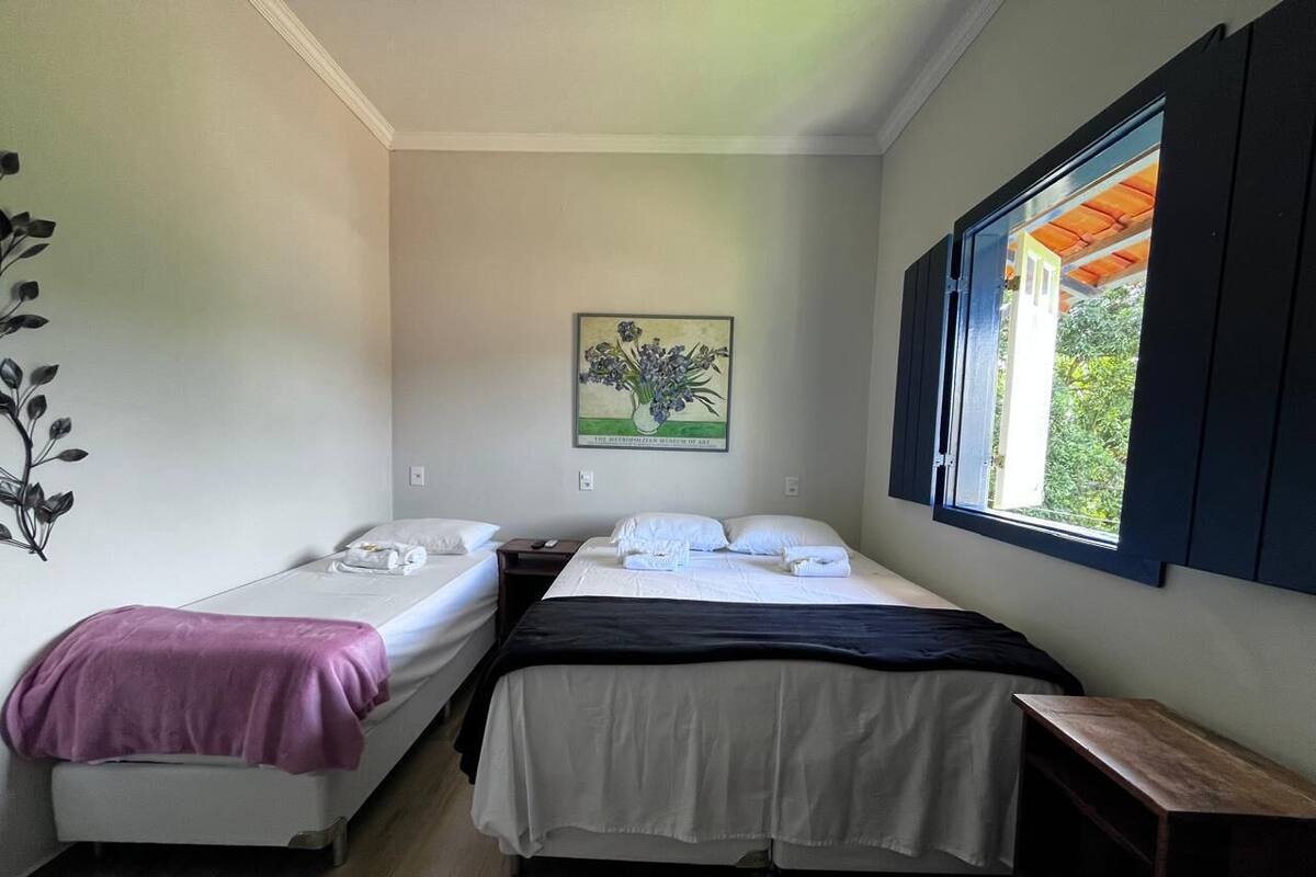 Quarto com duas camas, uma mesa pequena, janela com vista e um ornamento na parede.