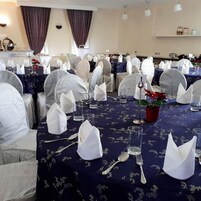 Salão de festas com mesas redondas dispostas para um evento formal, cada uma com identificação numérica, guardanapos brancos e talheres.
