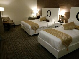 Quarto de hotel com duas camas, uma cadeira, mesa de cabeceira e abajur.