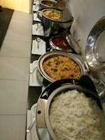 Buffet com diversos pratos, incluindo arroz, um prato à base de arroz e molho vermelho.