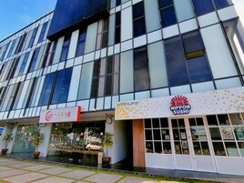 Um edifício moderno com fachada de vidro, um restaurante chamado 'NIPPON SUSHI' no andar térreo e uma placa com 'RESTORAN JAPON' sobre a entrada.