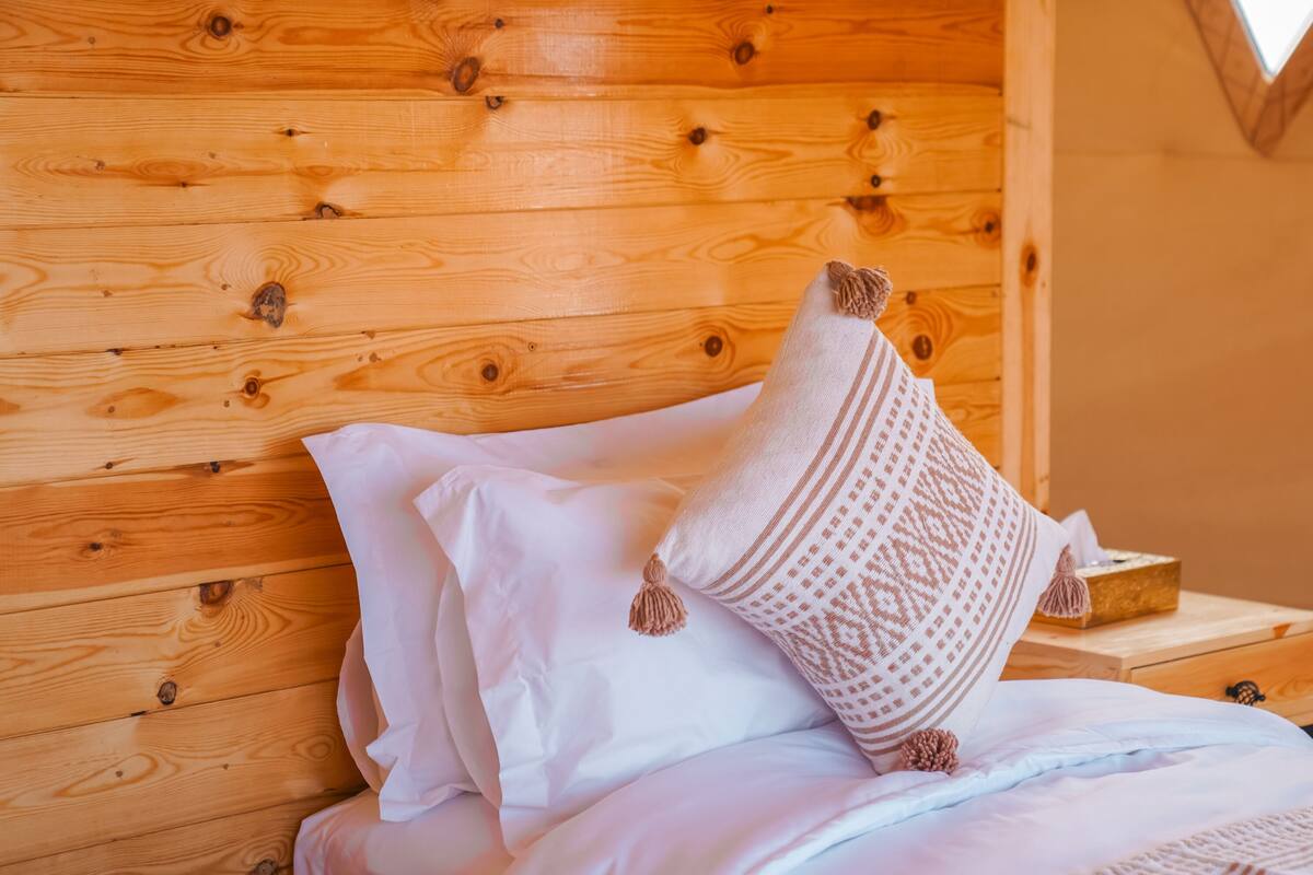 Quarto de cabana de madeira com cama, almofadas e mesa de cabeceira.