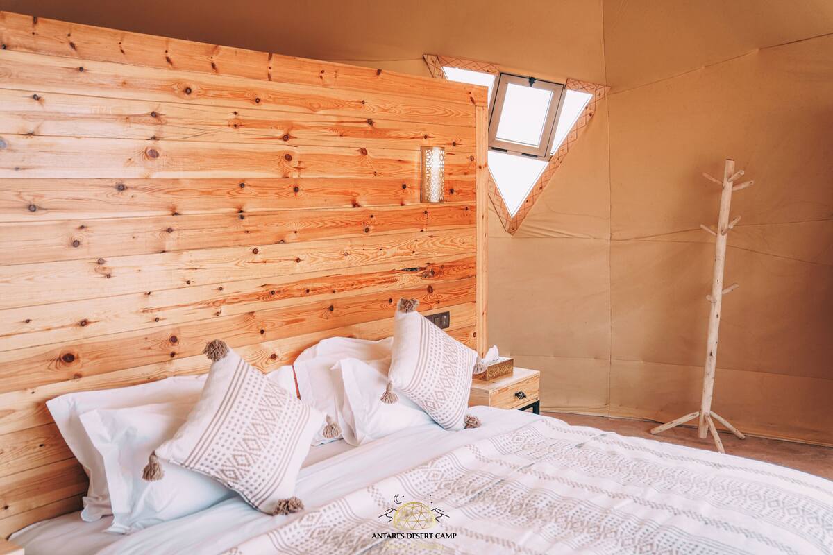Quarto com painéis de madeira, uma cama, almofadas e uma mesa de cabeceira.